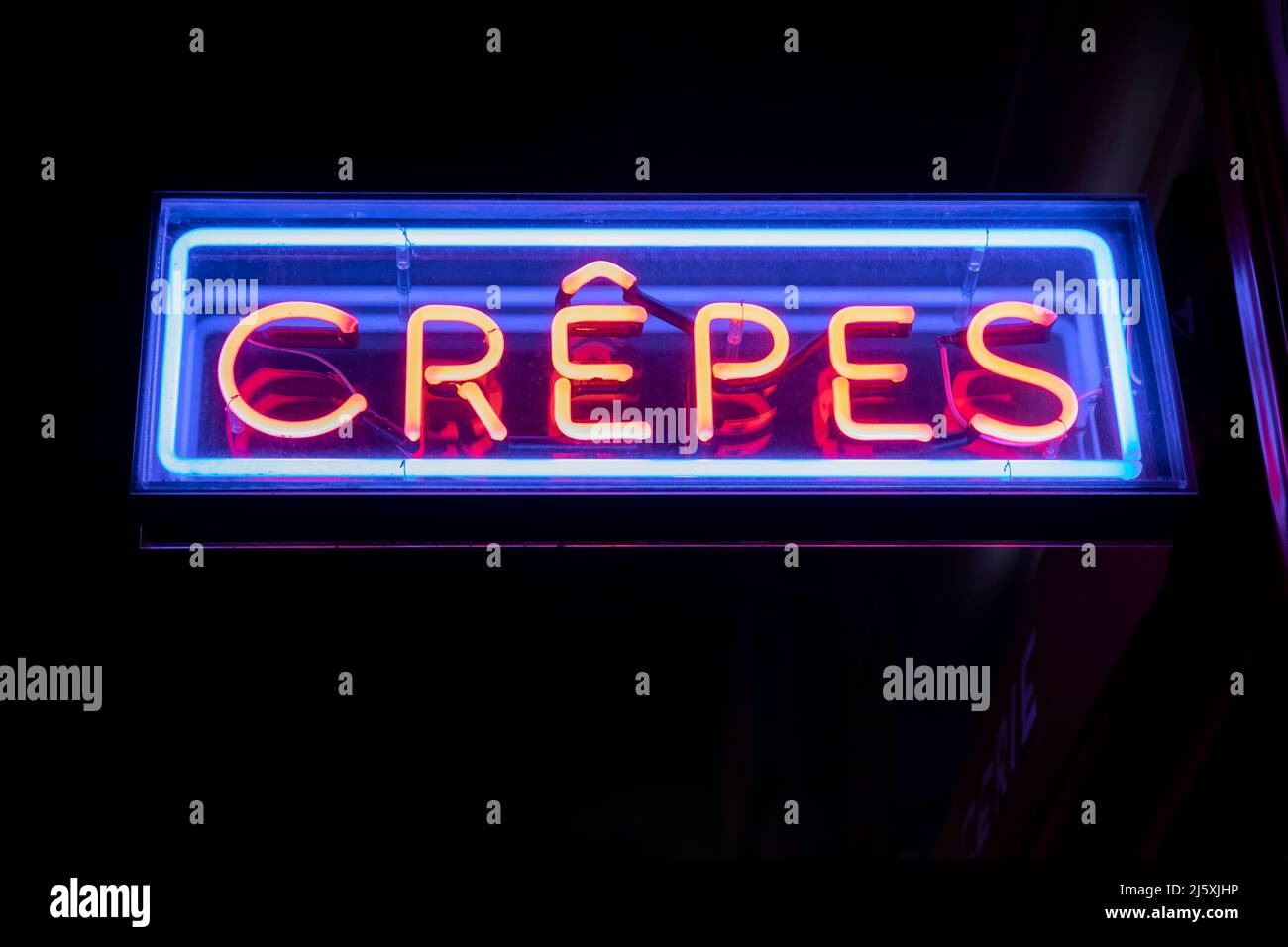 A crepe store with a bright neon blue and red sign glows in the dark on ...
