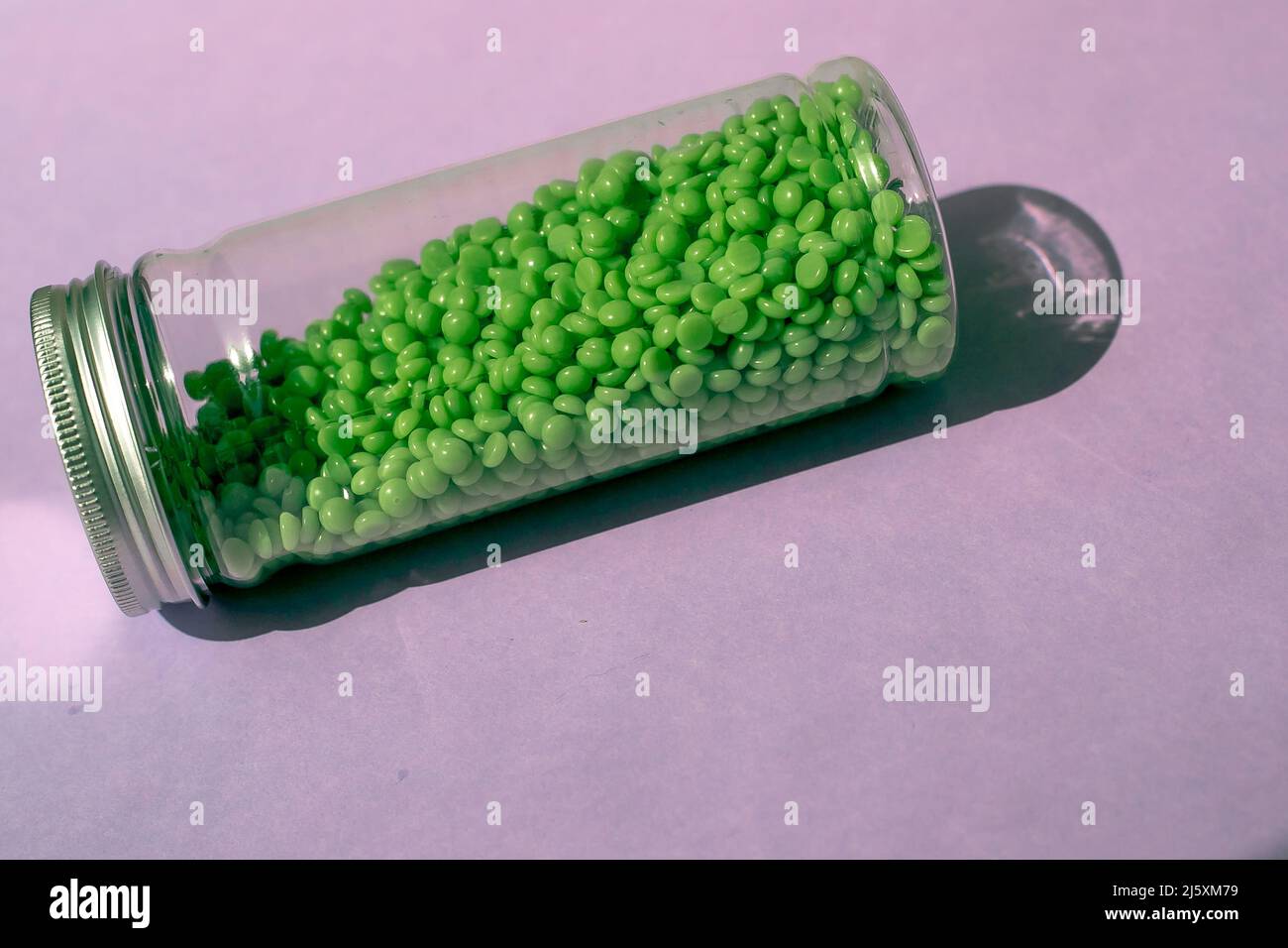 green wax for depilation in granules. on a purple background. jar with ...