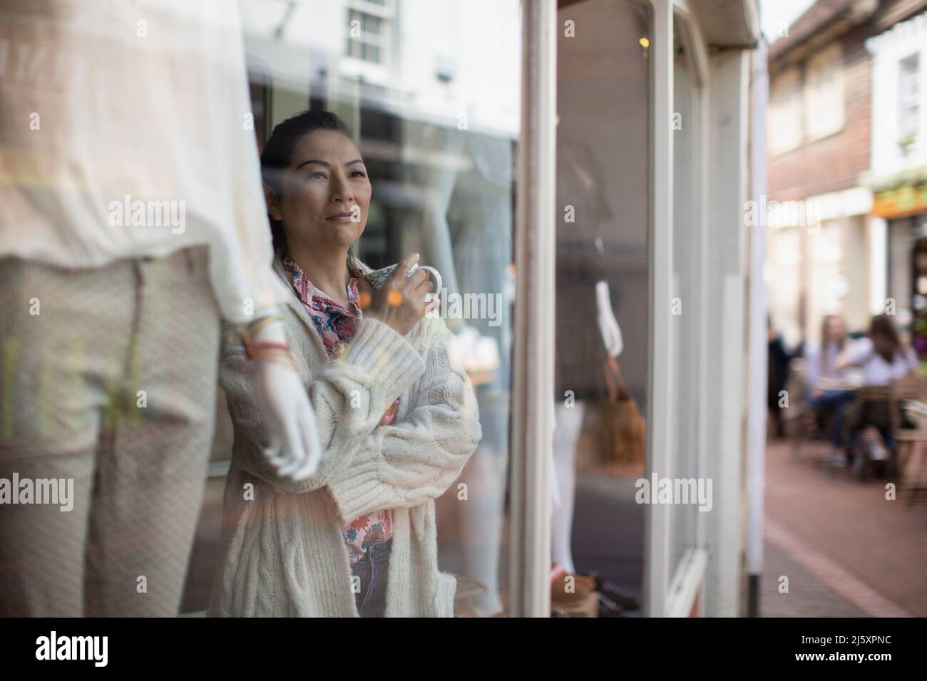 Female shop owner with tea looking out shop window Stock Photo - Alamy