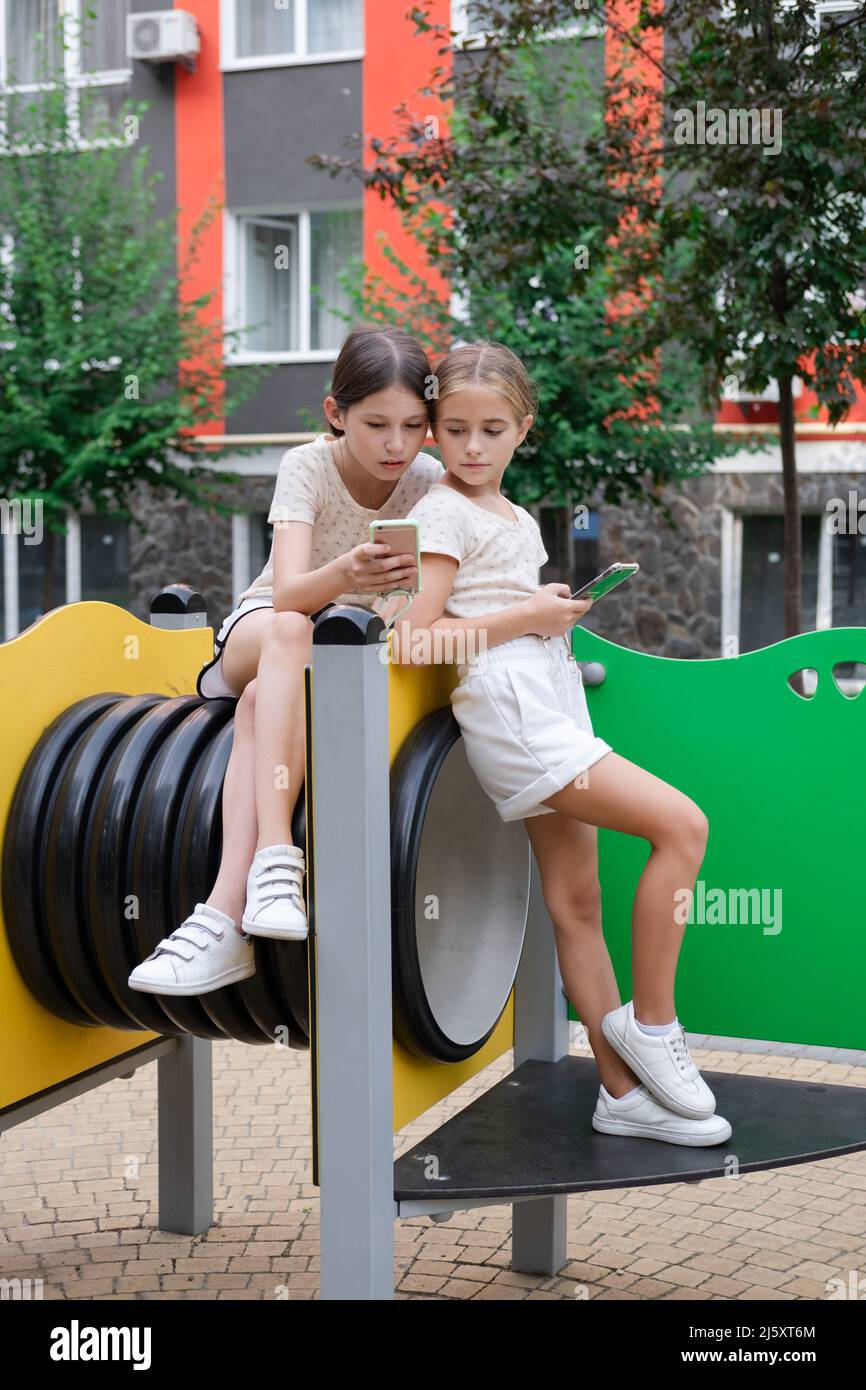 two charming teenage girls in identical clothes with smartphones ...