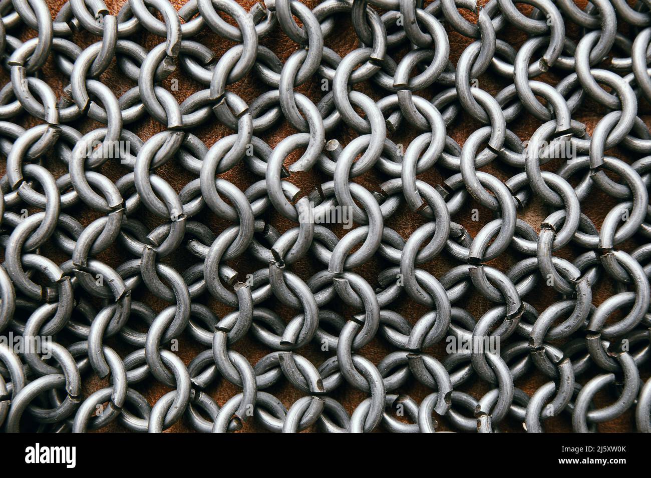Flat lay view of chain mail armor on brown leather. Metallic background ...