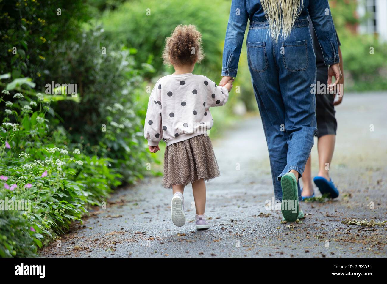 Mother and daughter holding hands walking on driveway Stock Photo - Alamy