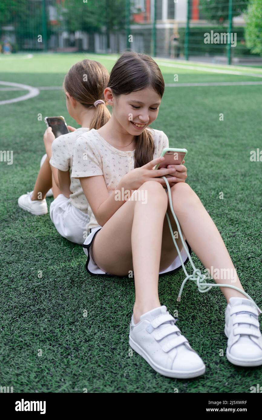 two charming teenage girls in identical clothes with smartphones ...