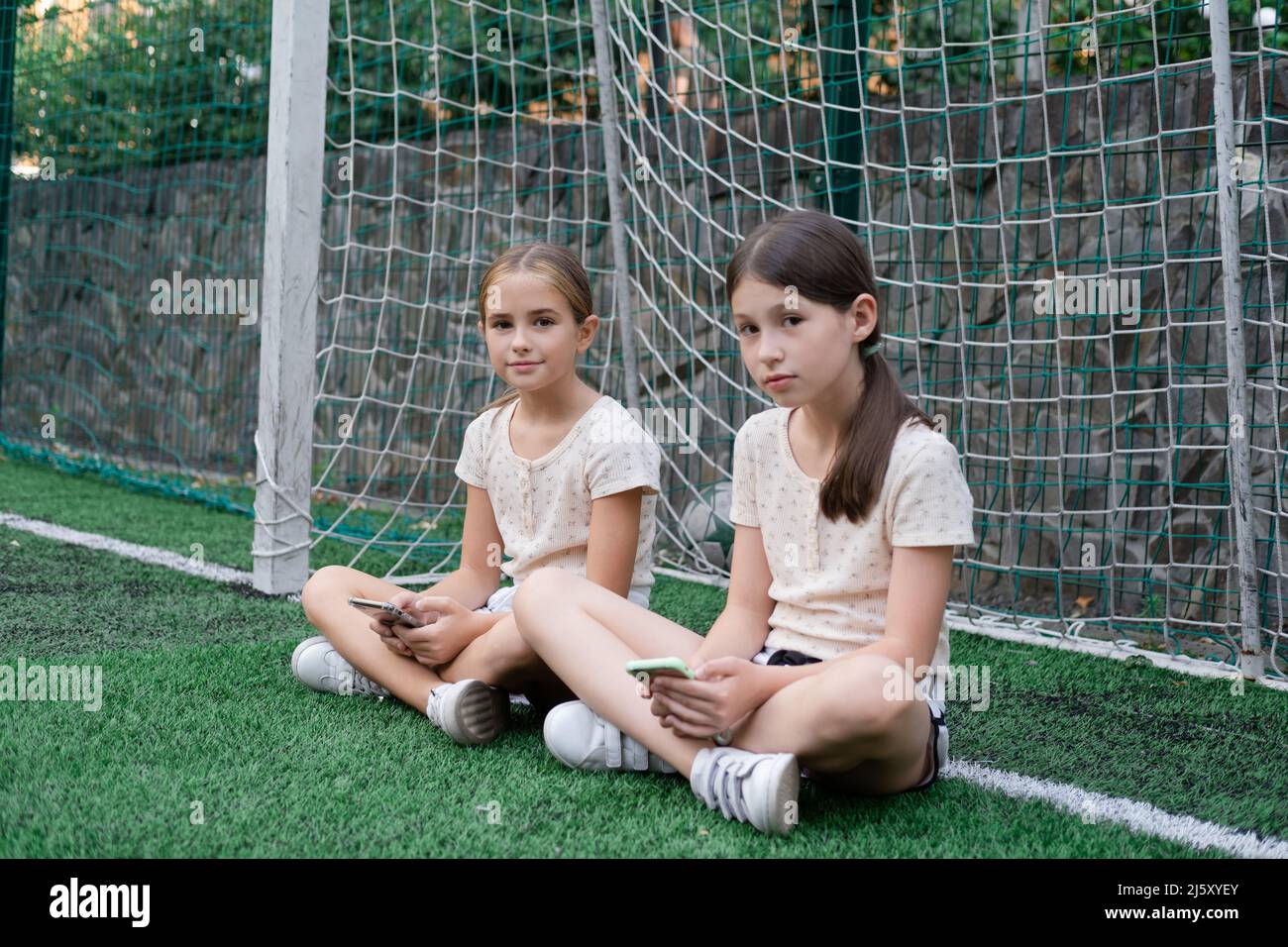 two charming teenage girls in identical clothes with smartphones ...