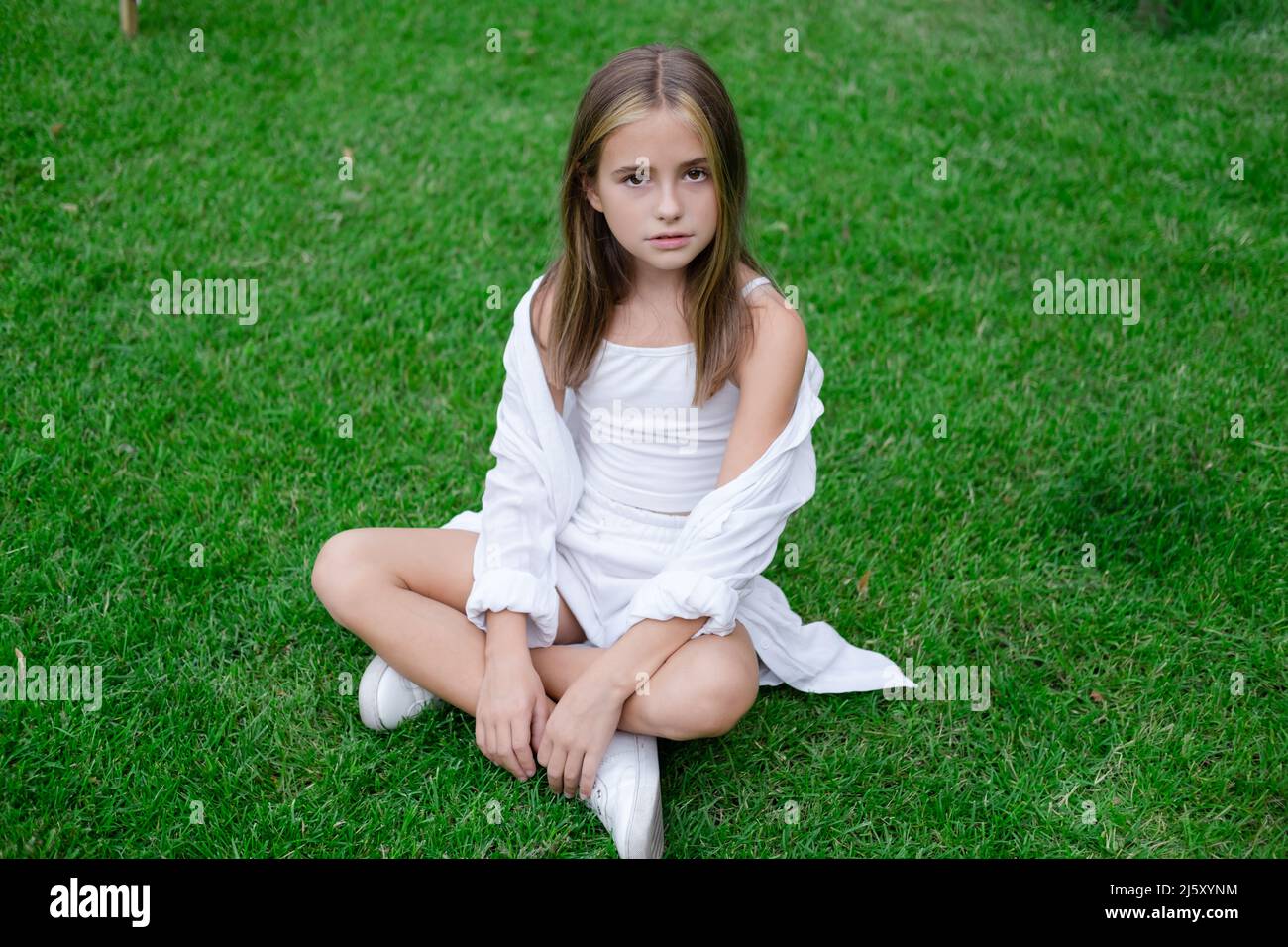 pretty tween girl in white clothes sitting on green grass outside in ...