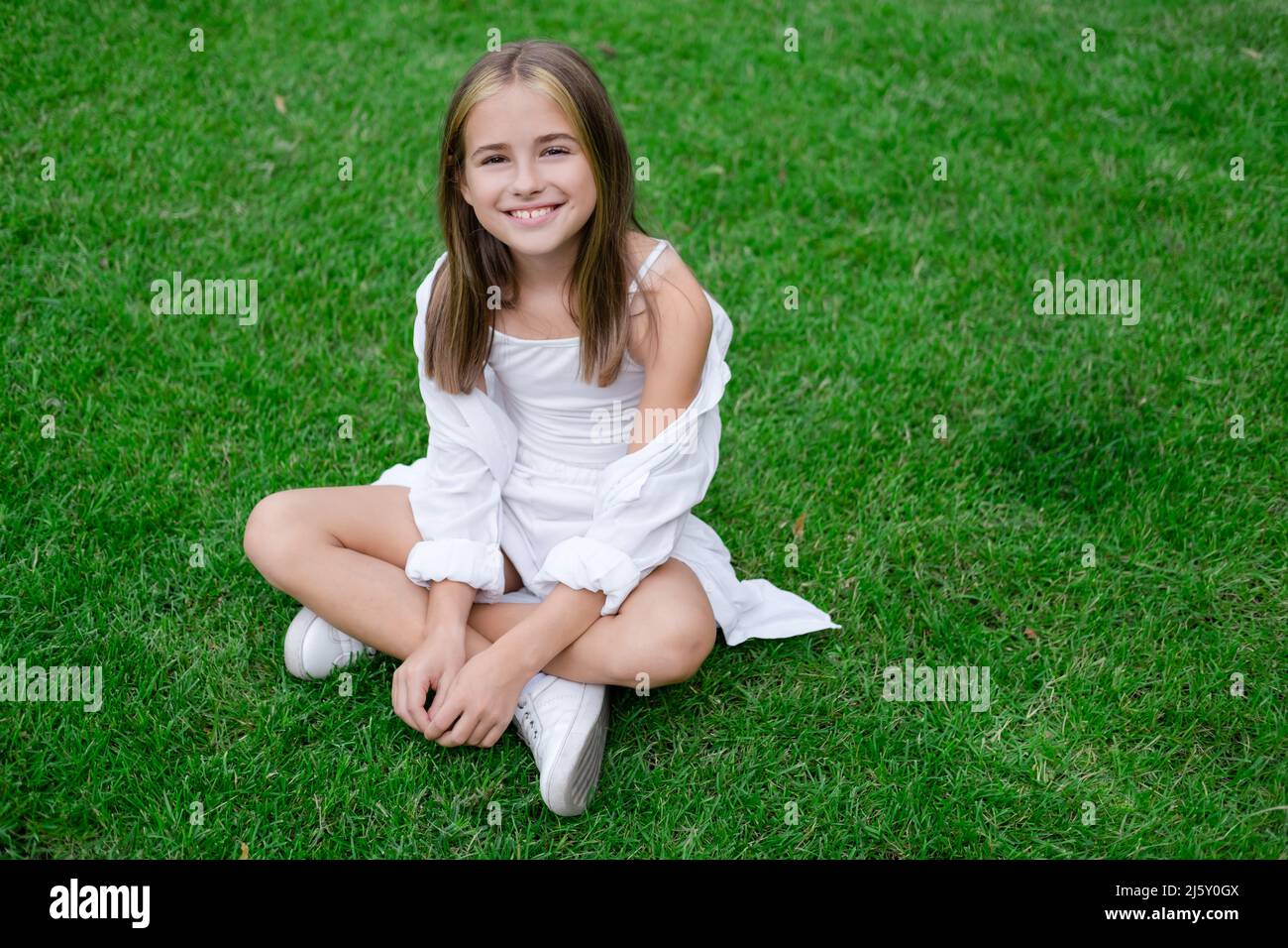 pretty tween girl in white clothes sitting on green grass outside in ...