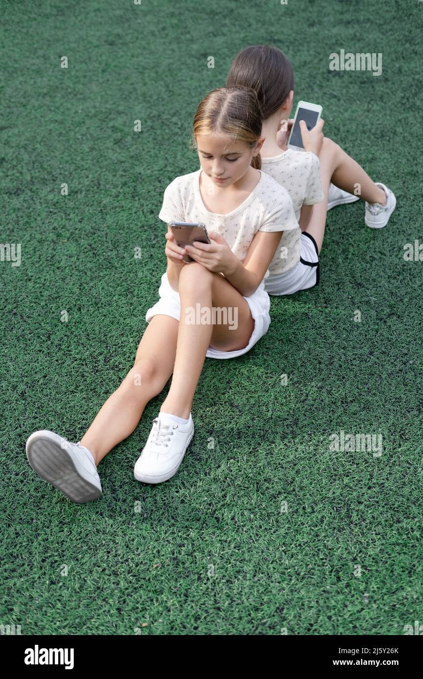 two charming teenage girls in identical clothes with smartphones ...
