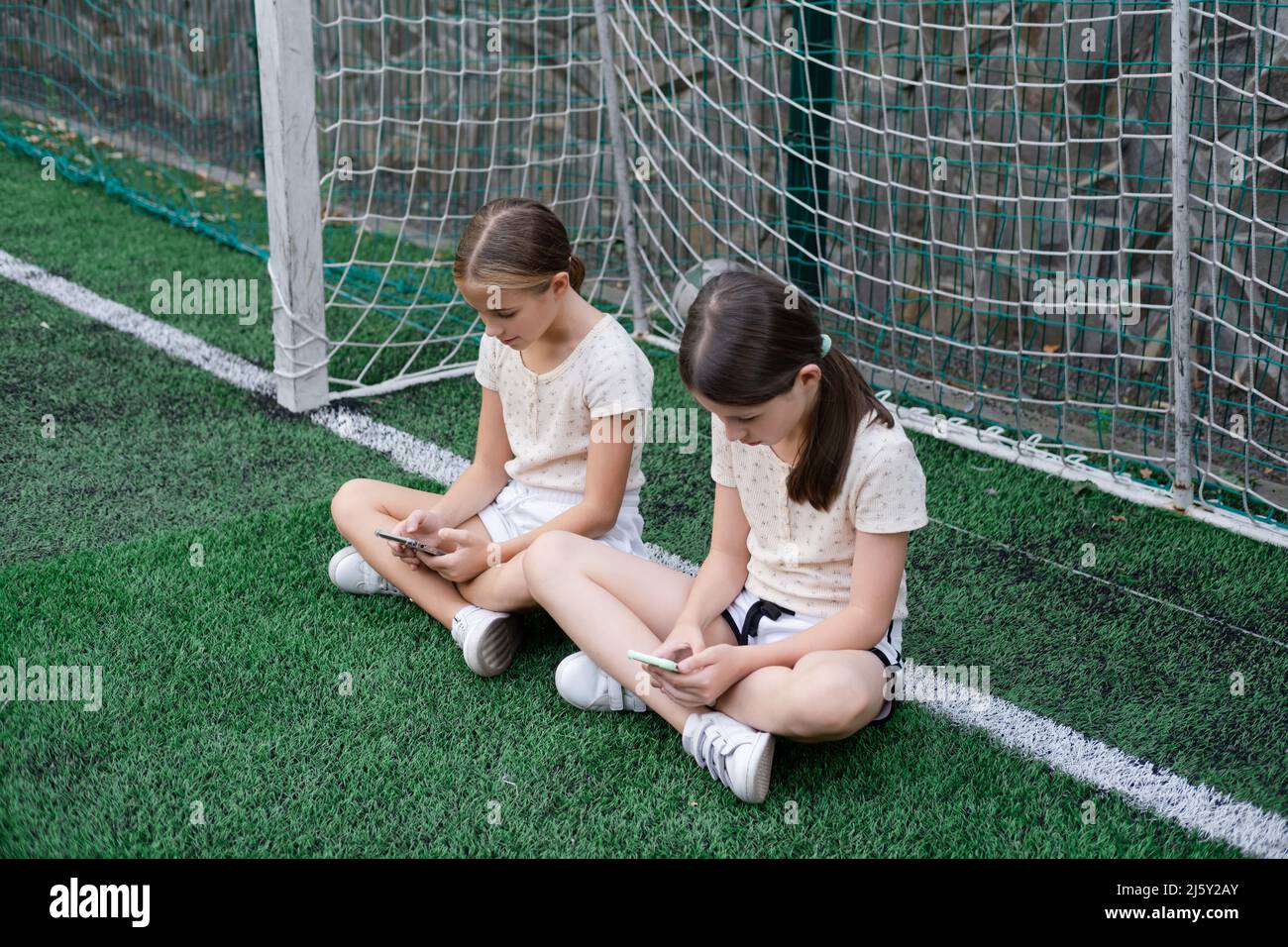 two charming teenage girls in identical clothes with smartphones ...