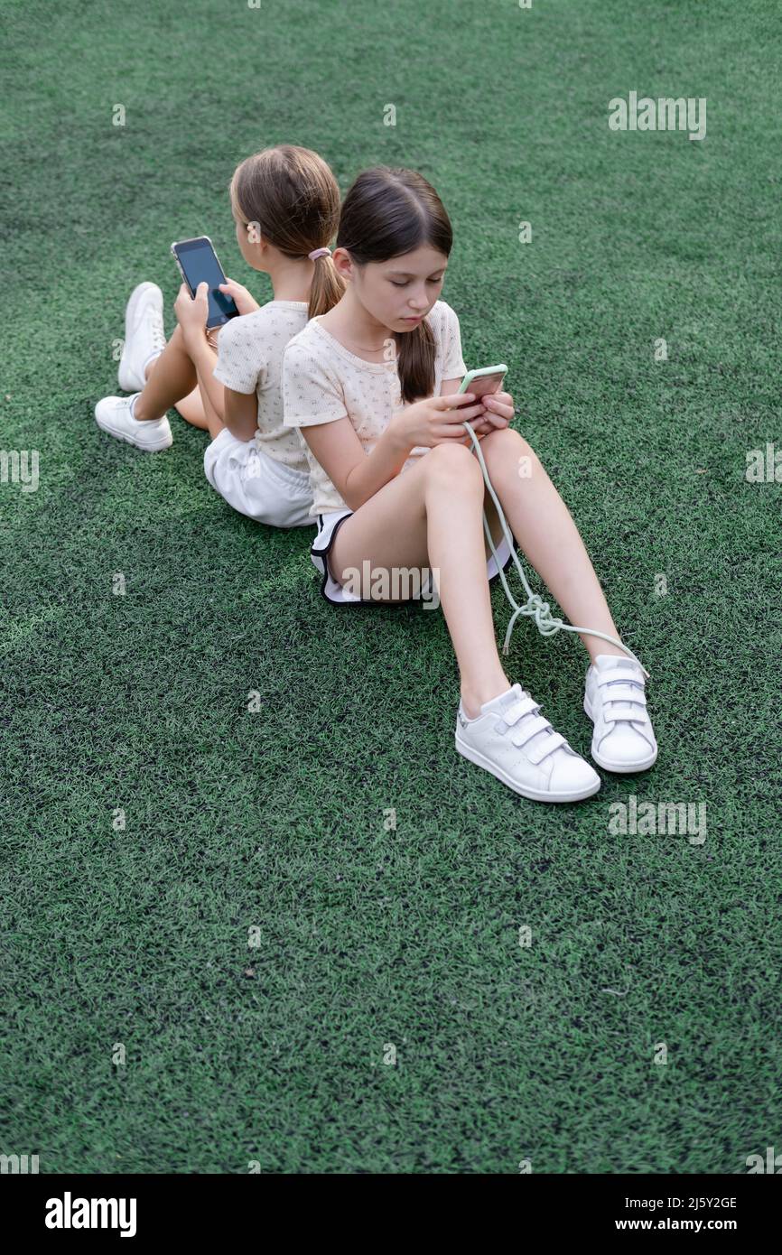 two charming teenage girls in identical clothes with smartphones ...