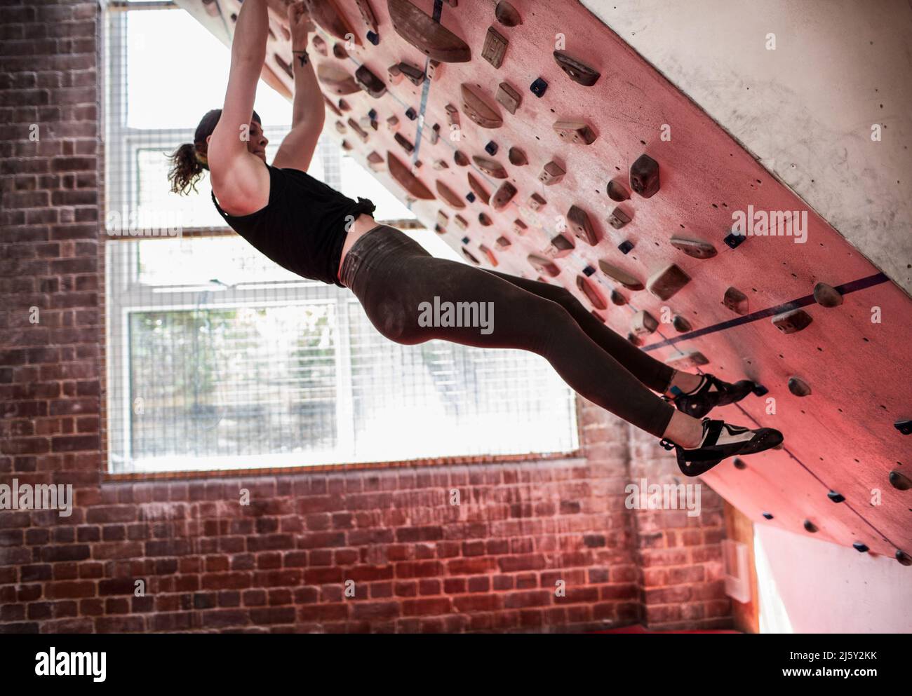 Young woman hanging from climbing wall Stock Photo - Alamy
