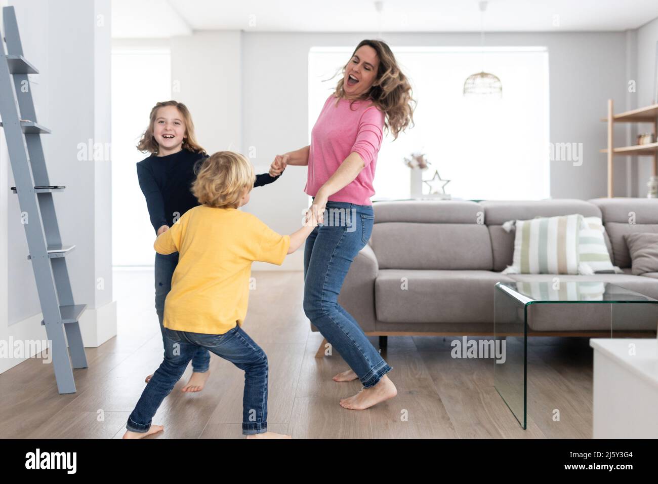 Full body of positive barefoot mother with cute children spinning ...
