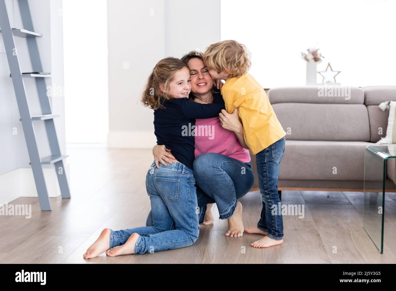 Full body of cute barefoot siblings kissing and hugging mother while ...