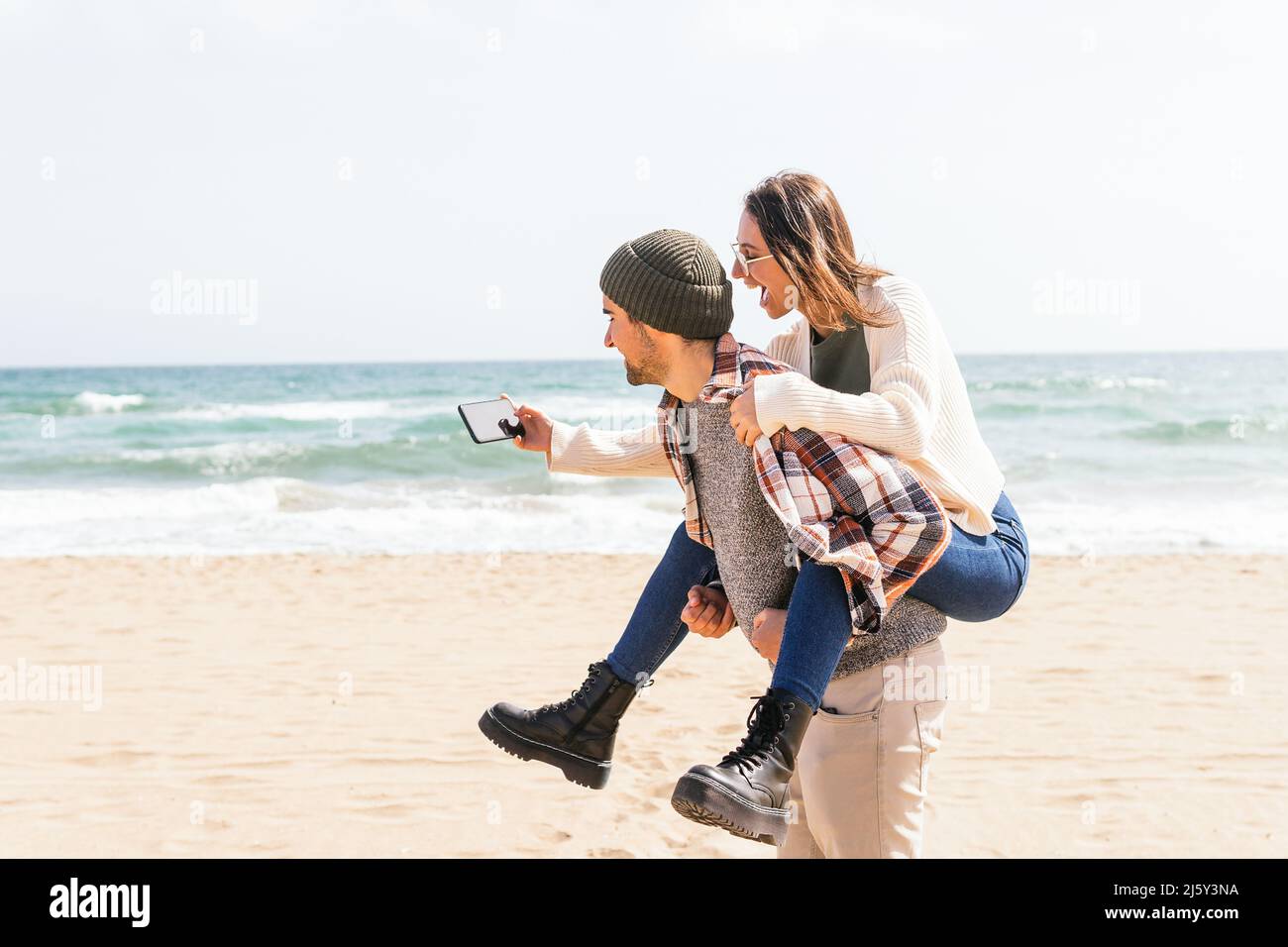 Side view of caring man giving piggyback ride to cheerful girlfriend on ...