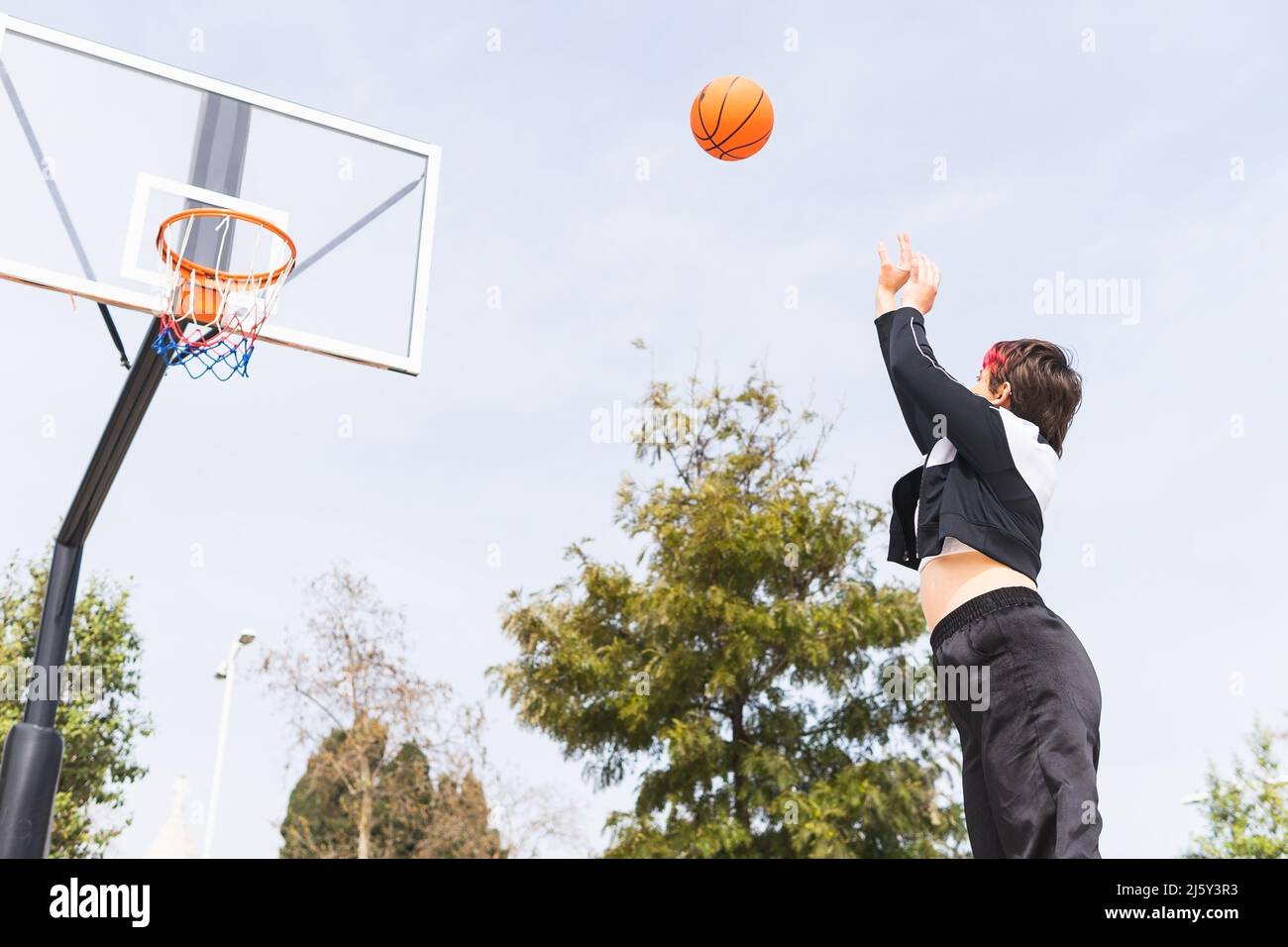 Low angle side view of female player throwing ball into hoop while ...