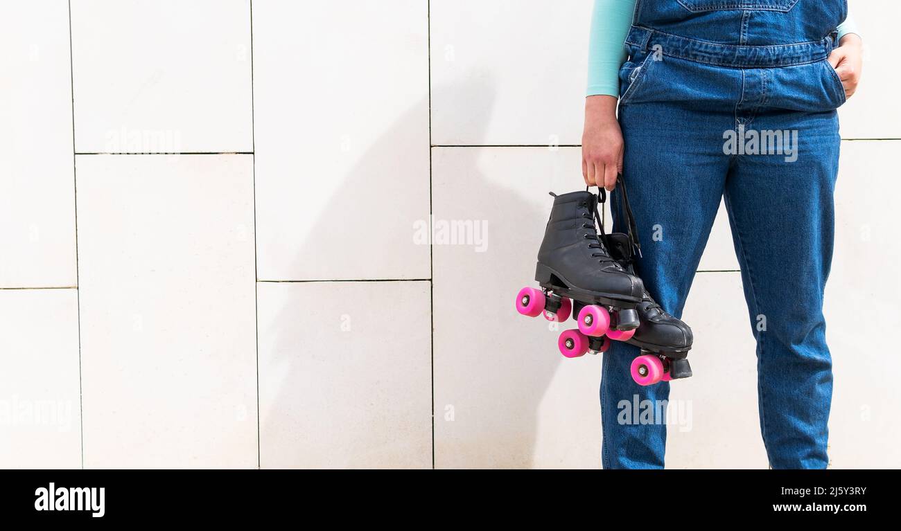 Side view of cropped Woman in denim overall holding roller skates while ...
