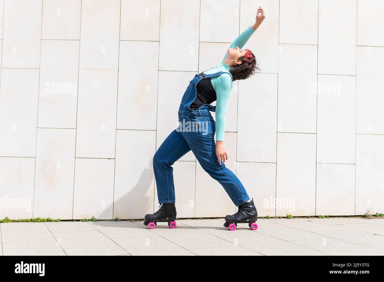 Lady with short hair in denim overall raising arm while dancing on quad ...