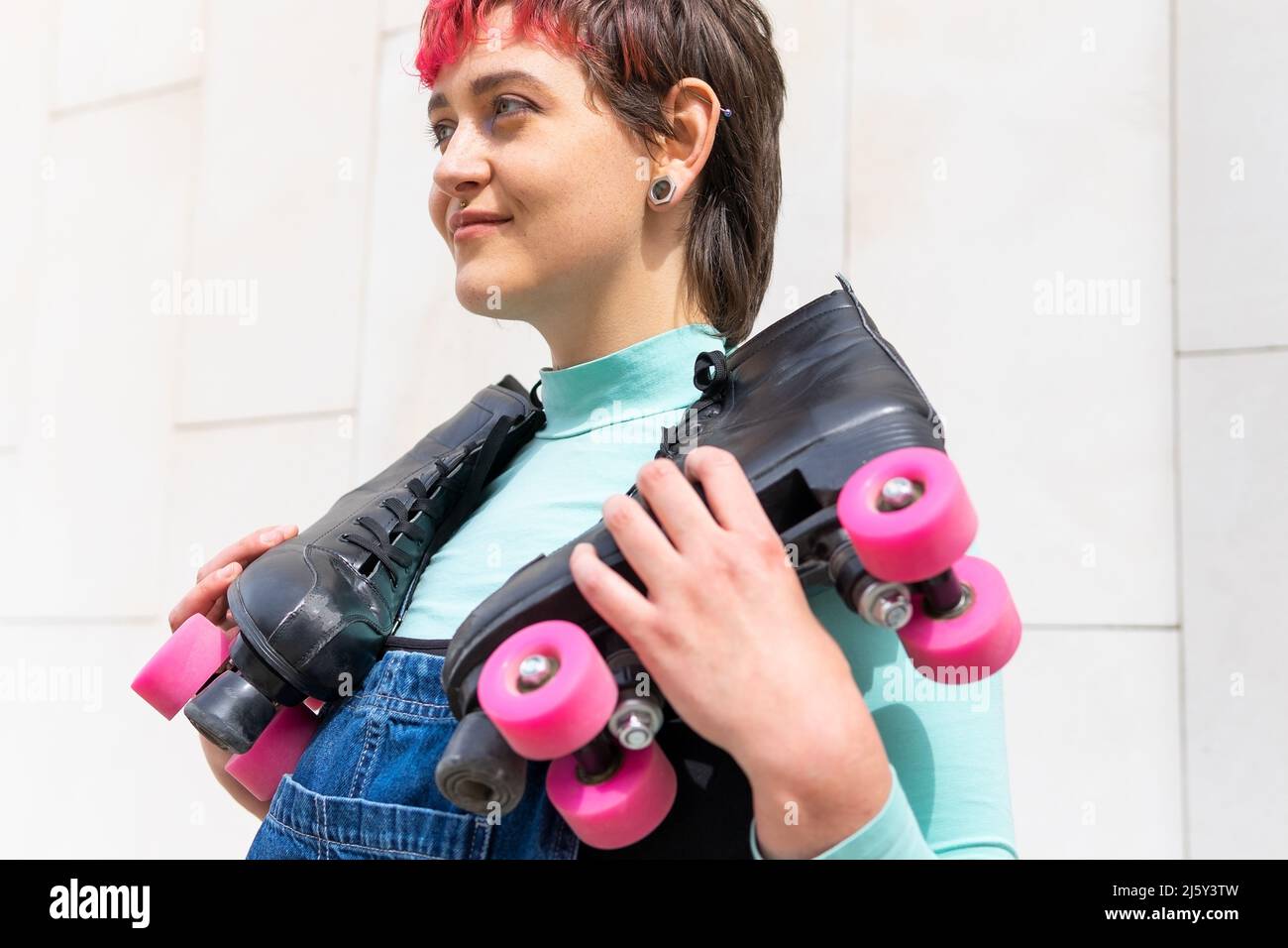 Side view of short haired Woman in denim overall holding roller skates ...