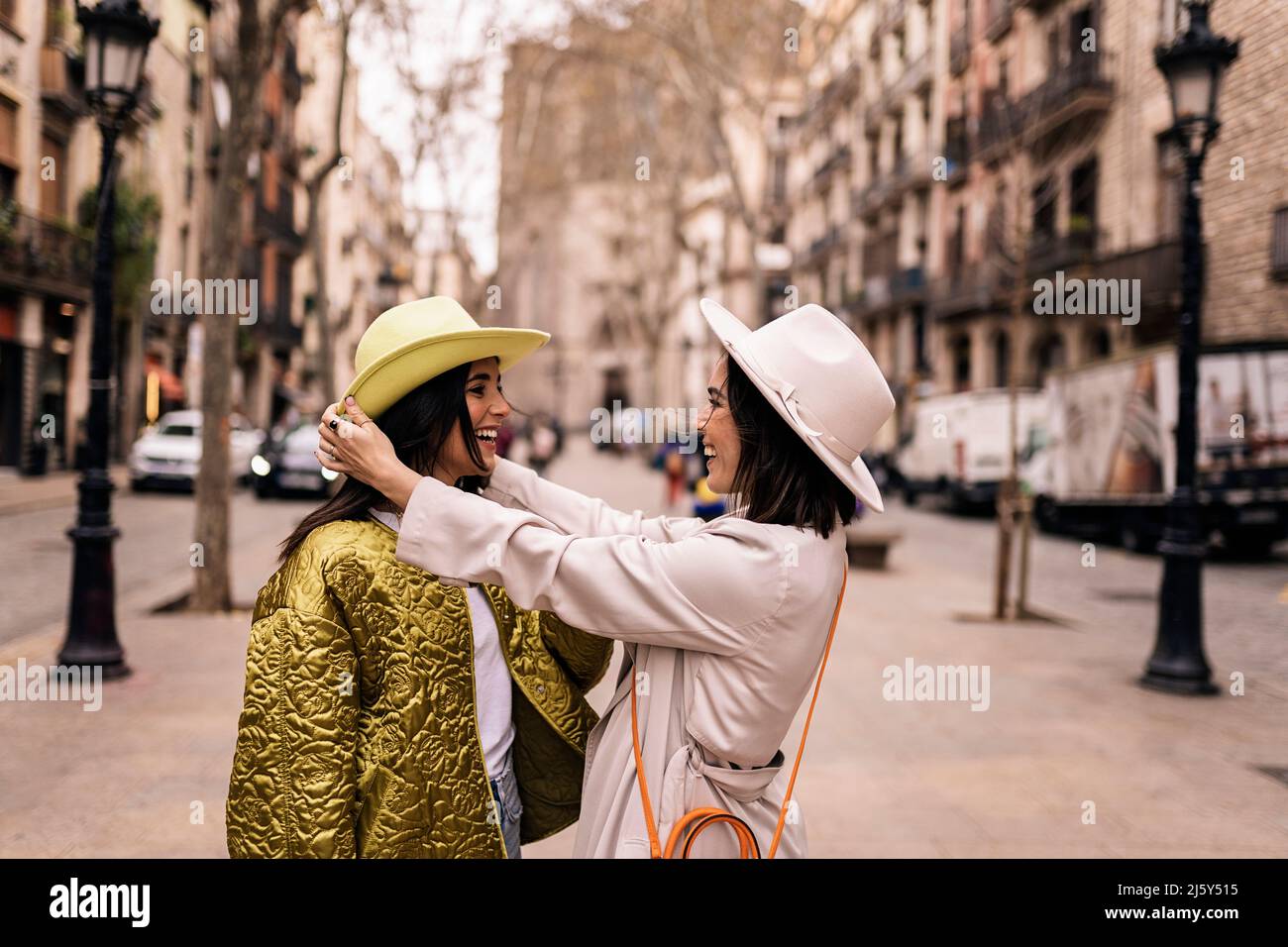 Side view of positive Woman fixing hat of female friend while standing ...