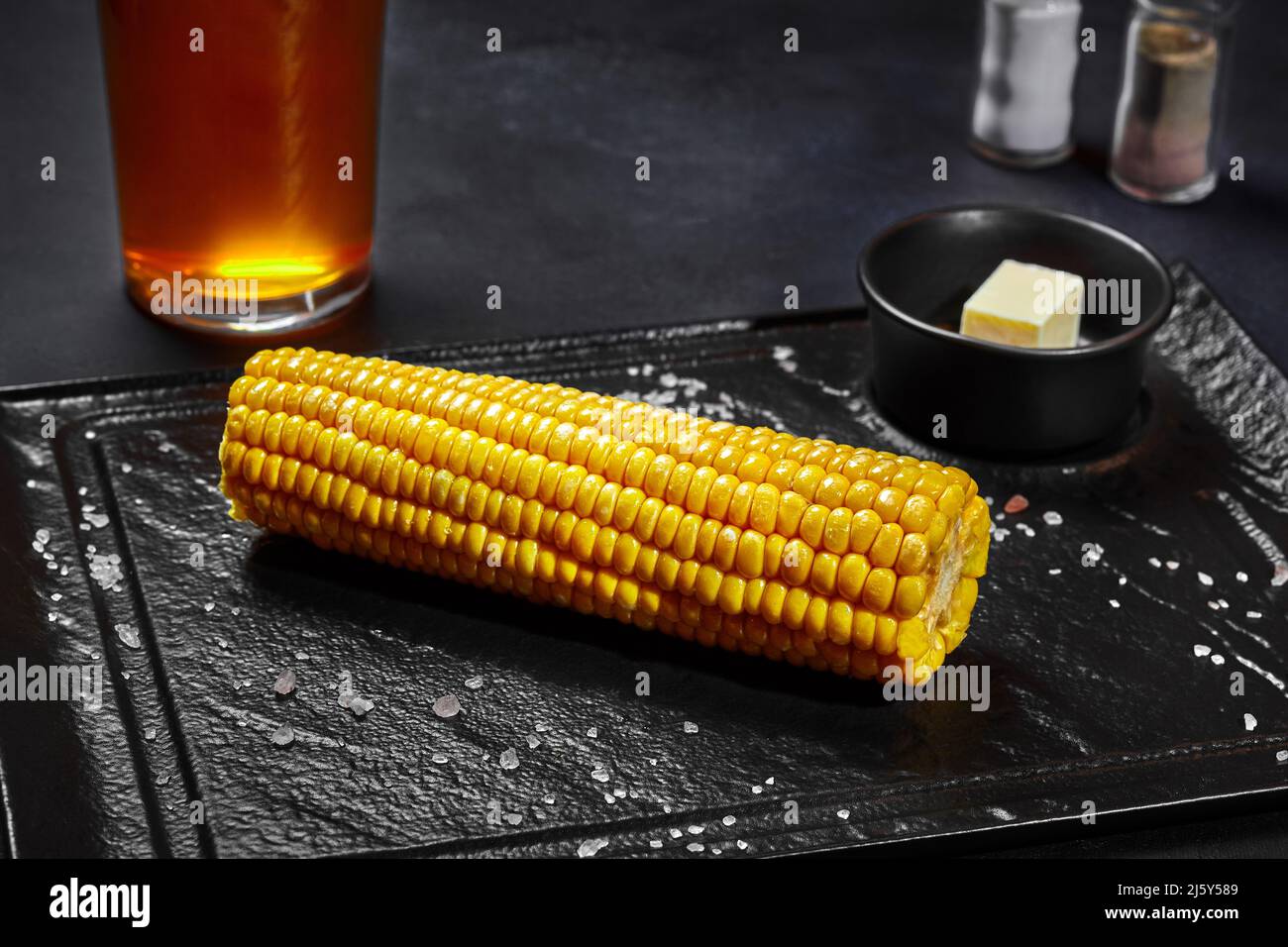 Cooked ear of sweet corn with salt and butter on black slate board ...