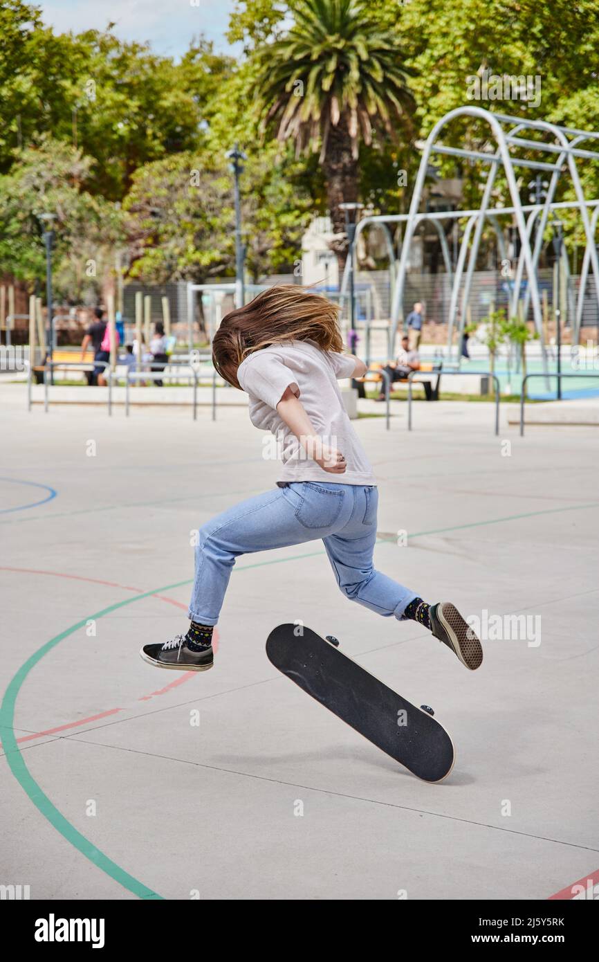 Full body back view of active female jumping on skateboard while ...