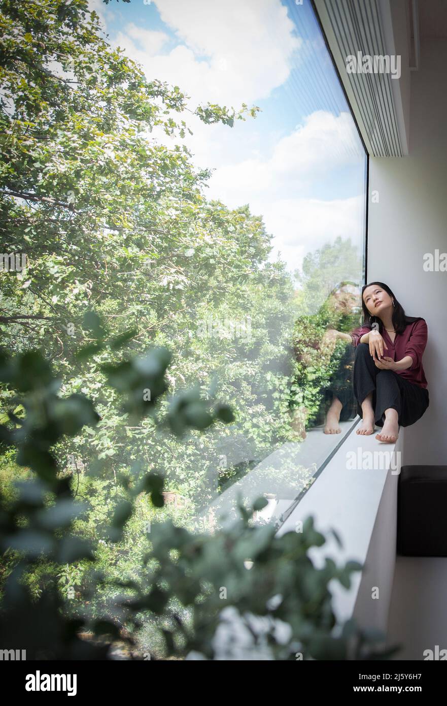 Thoughtful young woman looking at trees from window at home Stock Photo ...