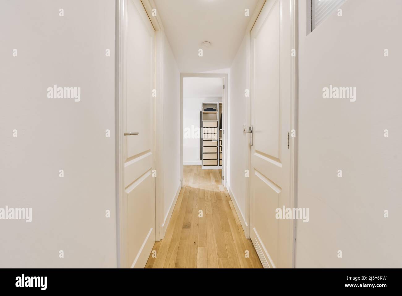 White closed room doors in narrow corridor leading to opened room with ...