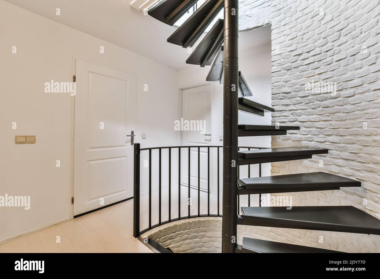 Black steps of long spiral stairway placed at white brick wall in ...