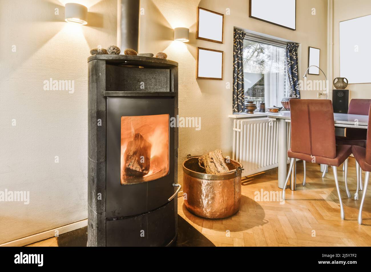 Chairs at table near black metal furnace with burning firewood in light ...