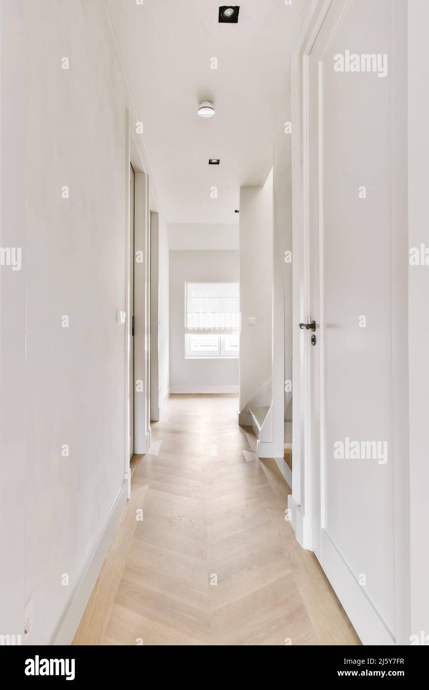 Empty narrow hallway with white walls and doors and beige laminated ...