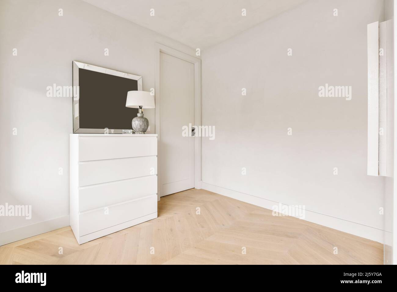 White chest of drawers with decorative frame and lamp placed at wall in ...