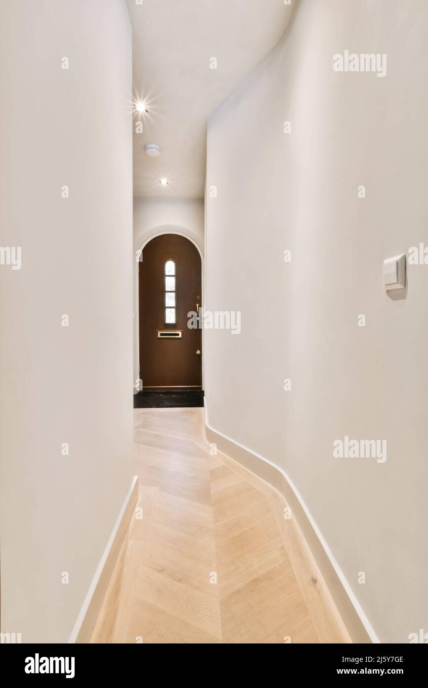 Empty narrow corridor with parquet floor and white walls leading to ...