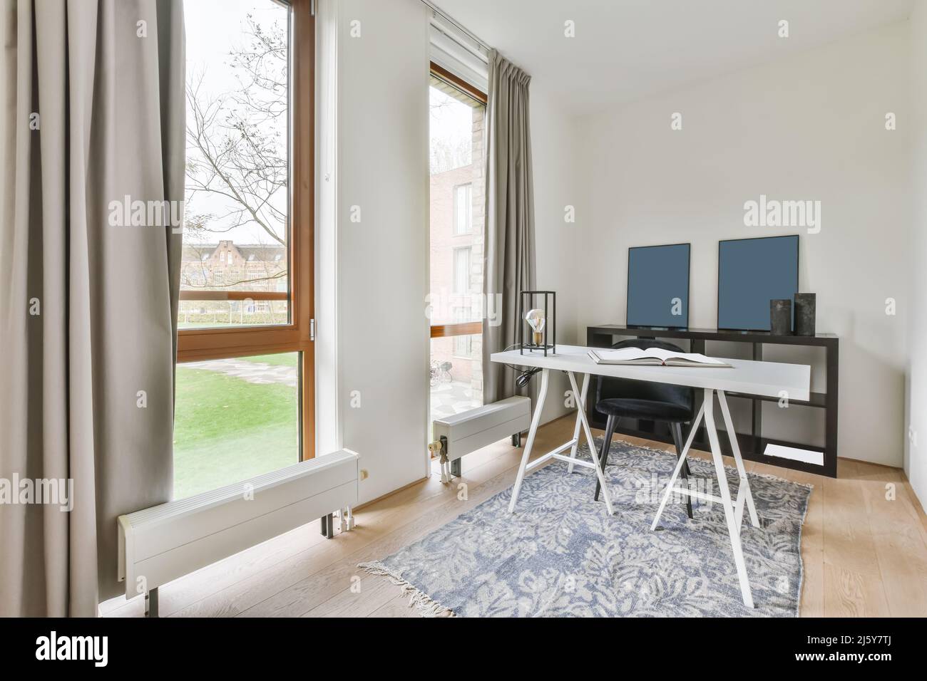 White table with opened book placed on rug near windows in light ...