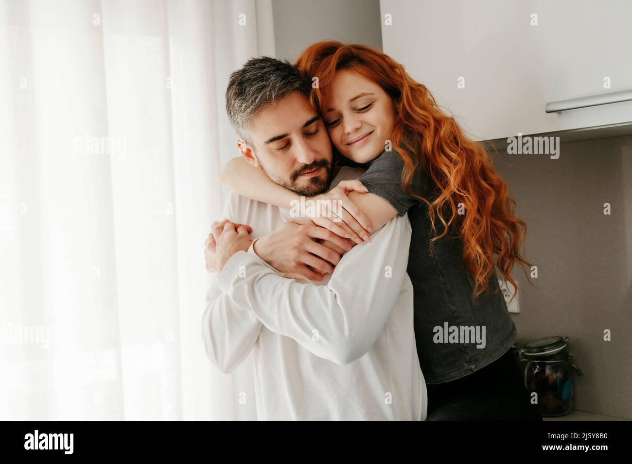 Romantic couple in casual wear embracing with closed eyes while ...