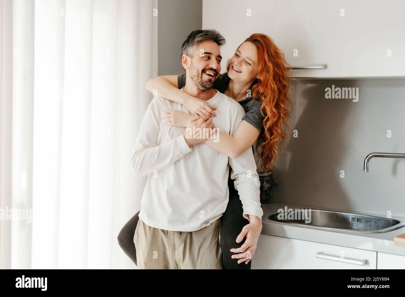 Romantic cheerful couple in casual wear embracing while cuddling near ...