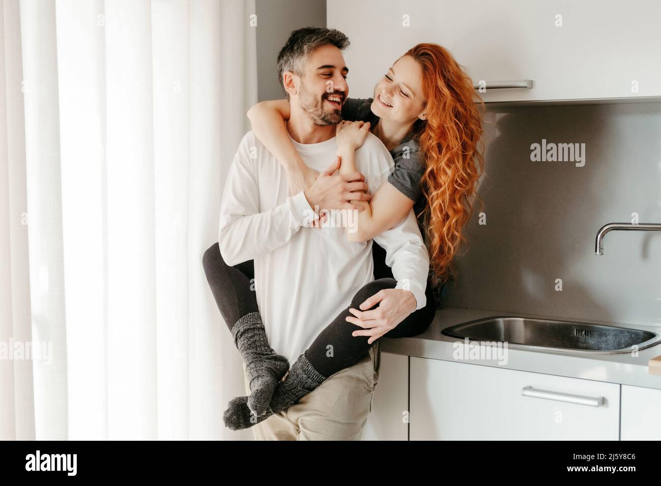 Romantic cheerful couple in casual wear embracing while cuddling near ...