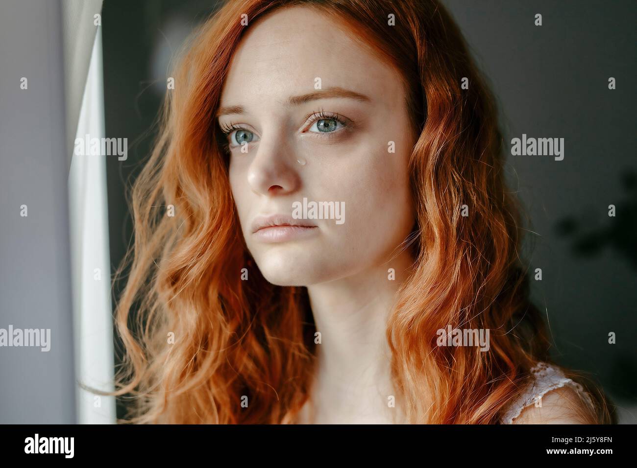 Side view of melancholic young female with curly red hair looking out ...