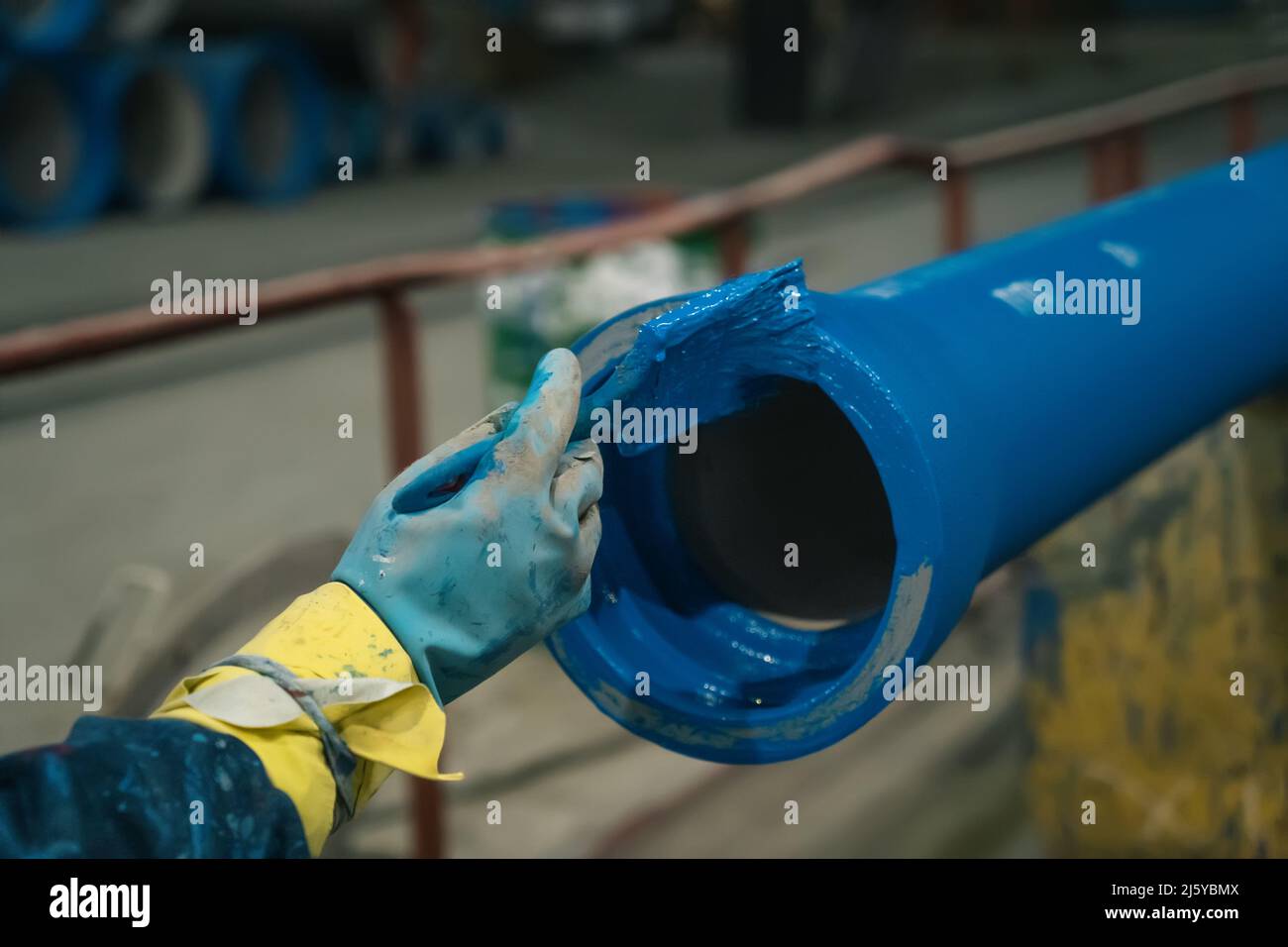 Worker hand painting in blue color steel pipe with brush in factory ...