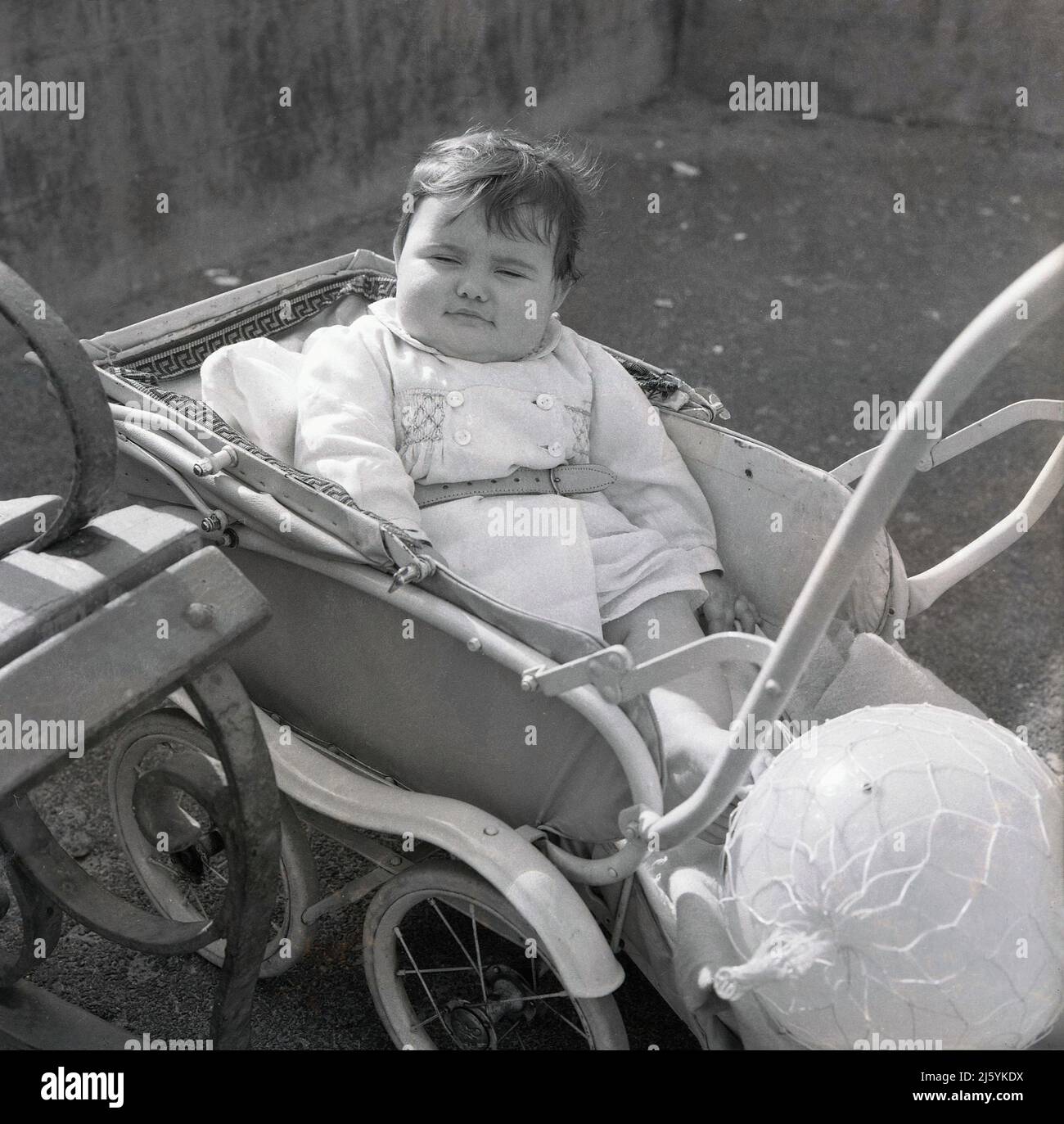 1961, historical, infant child resting in a metal framed pushchair of ...