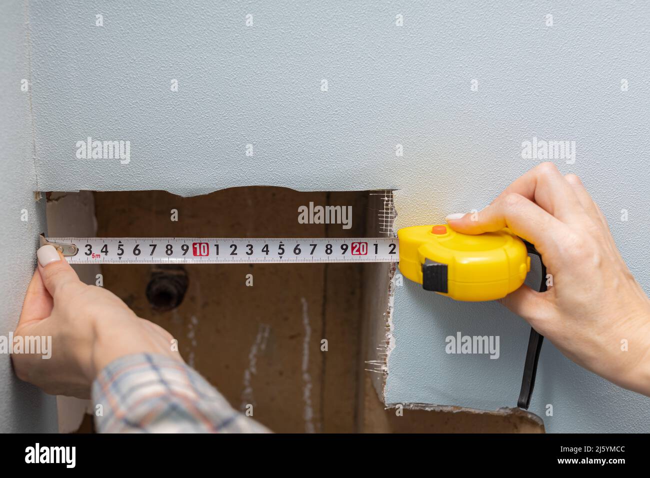 a woman measures a hole in the wall with a tape measure. High quality ...
