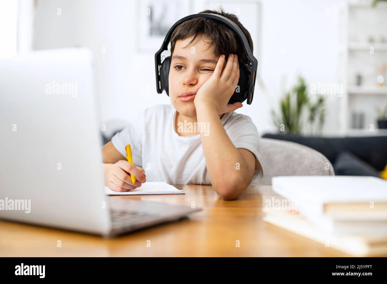 Tired schoolboy doing homework and listening music in the headphones ...
