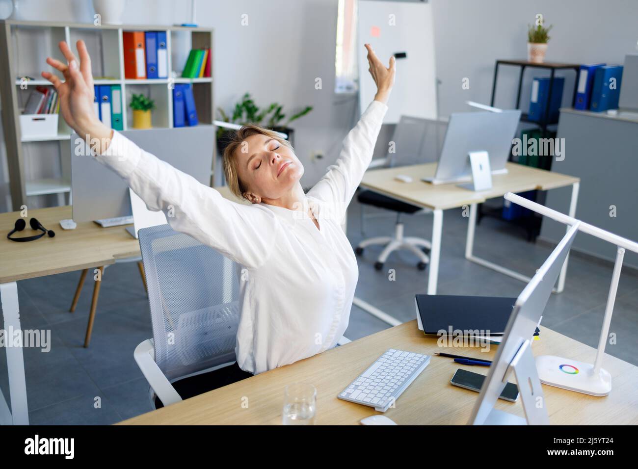 Mature businesswoman stretches while sitting at her desk in the office ...