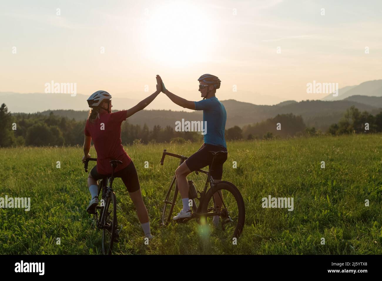Road cyclists, man and woman, stopping at a grassy hill to celebrate ...