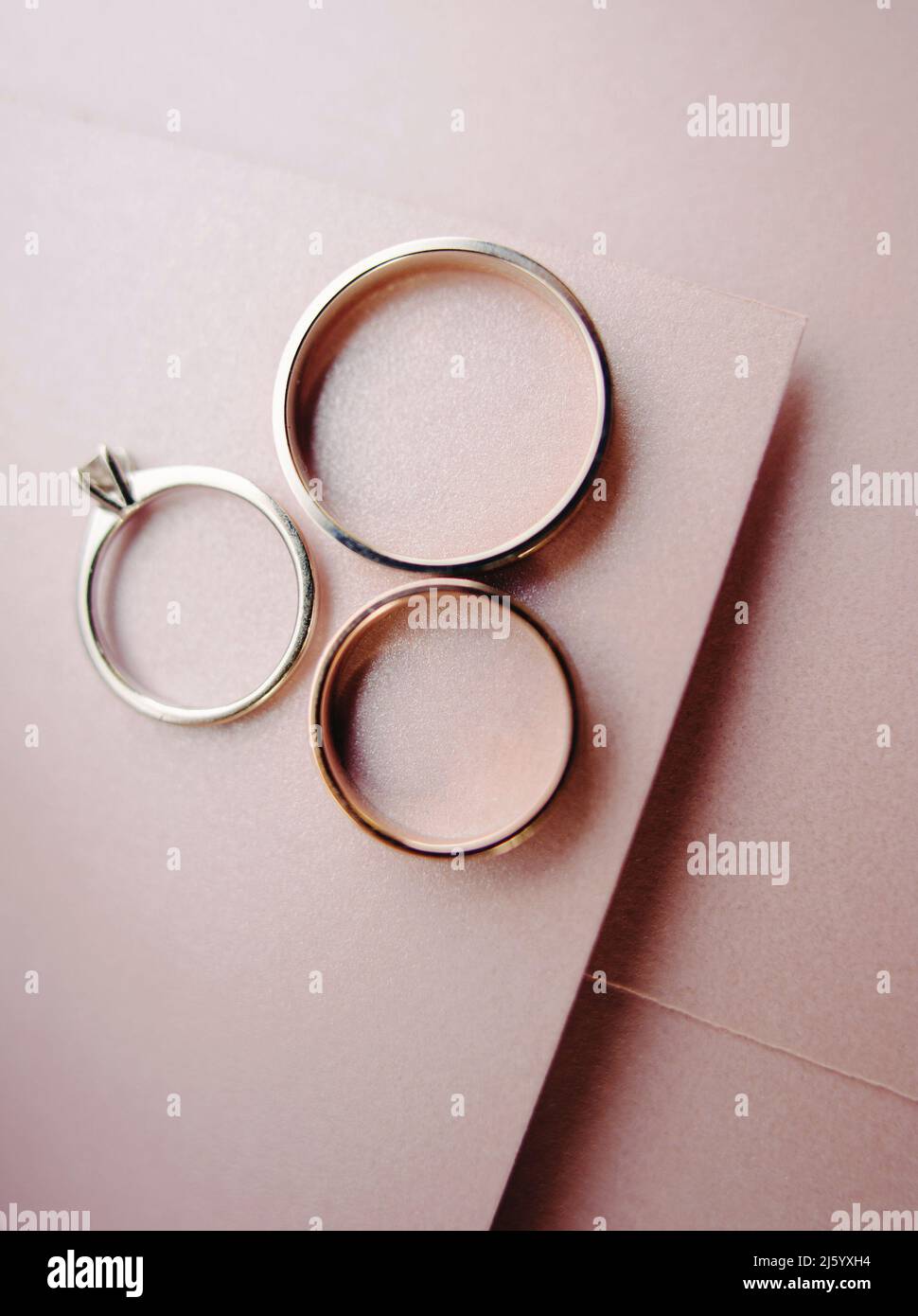 Wedding band and golden engagement ring on rosy paper background, close ...