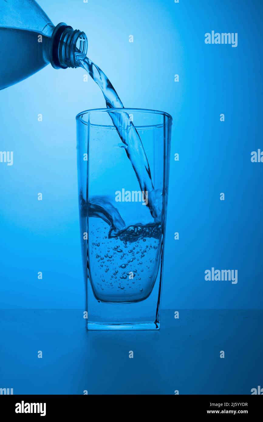 Ecologically clean water is poured from a bottle into a glass on a blue ...