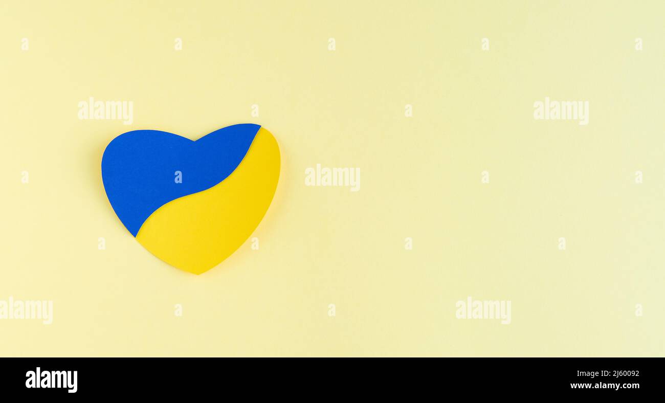 Heart cut out of paper with Ukrainian flag colors on yellow background ...