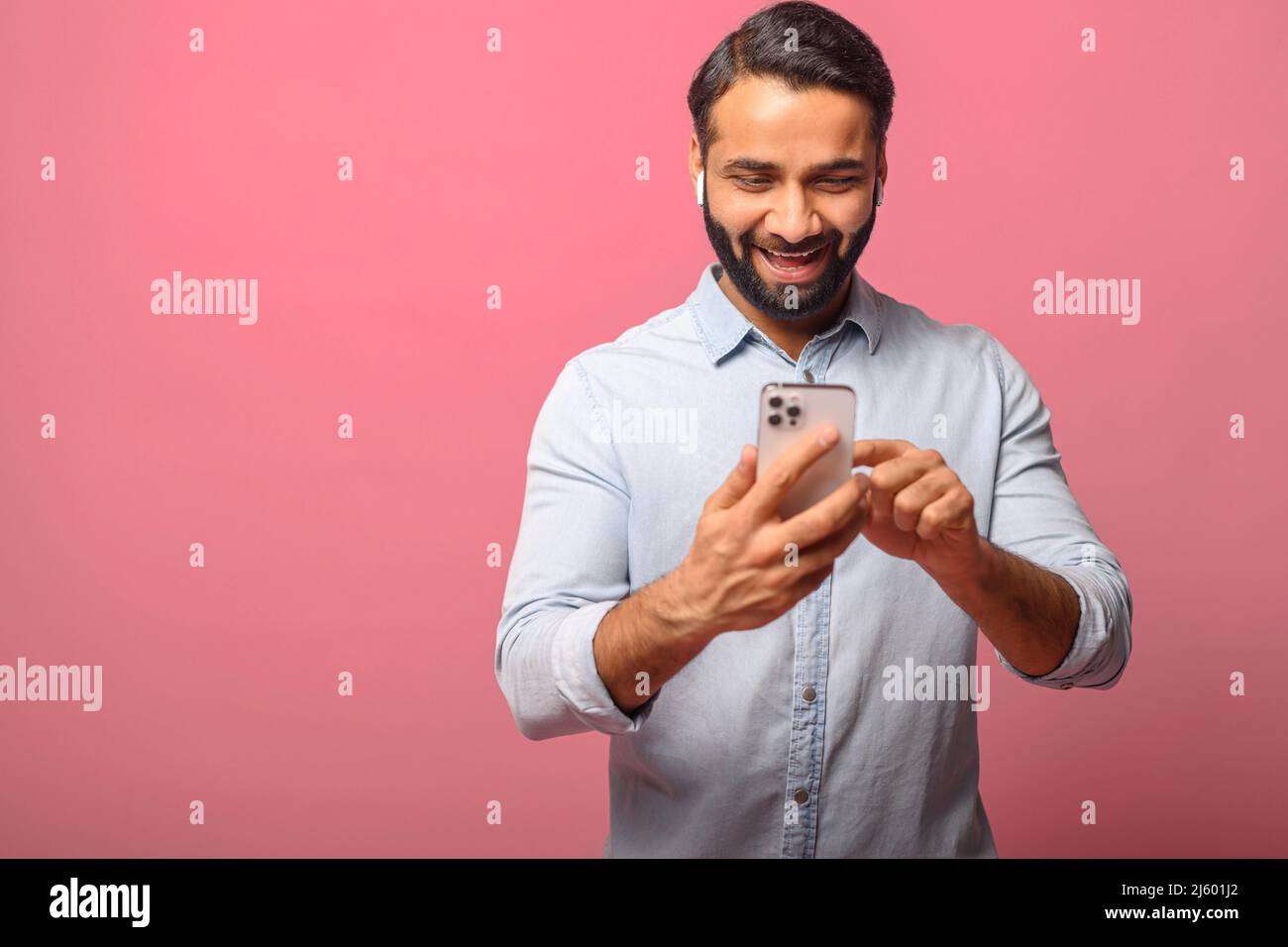 Smiling Indian man with airpods holding and using smartphone, carefree ...