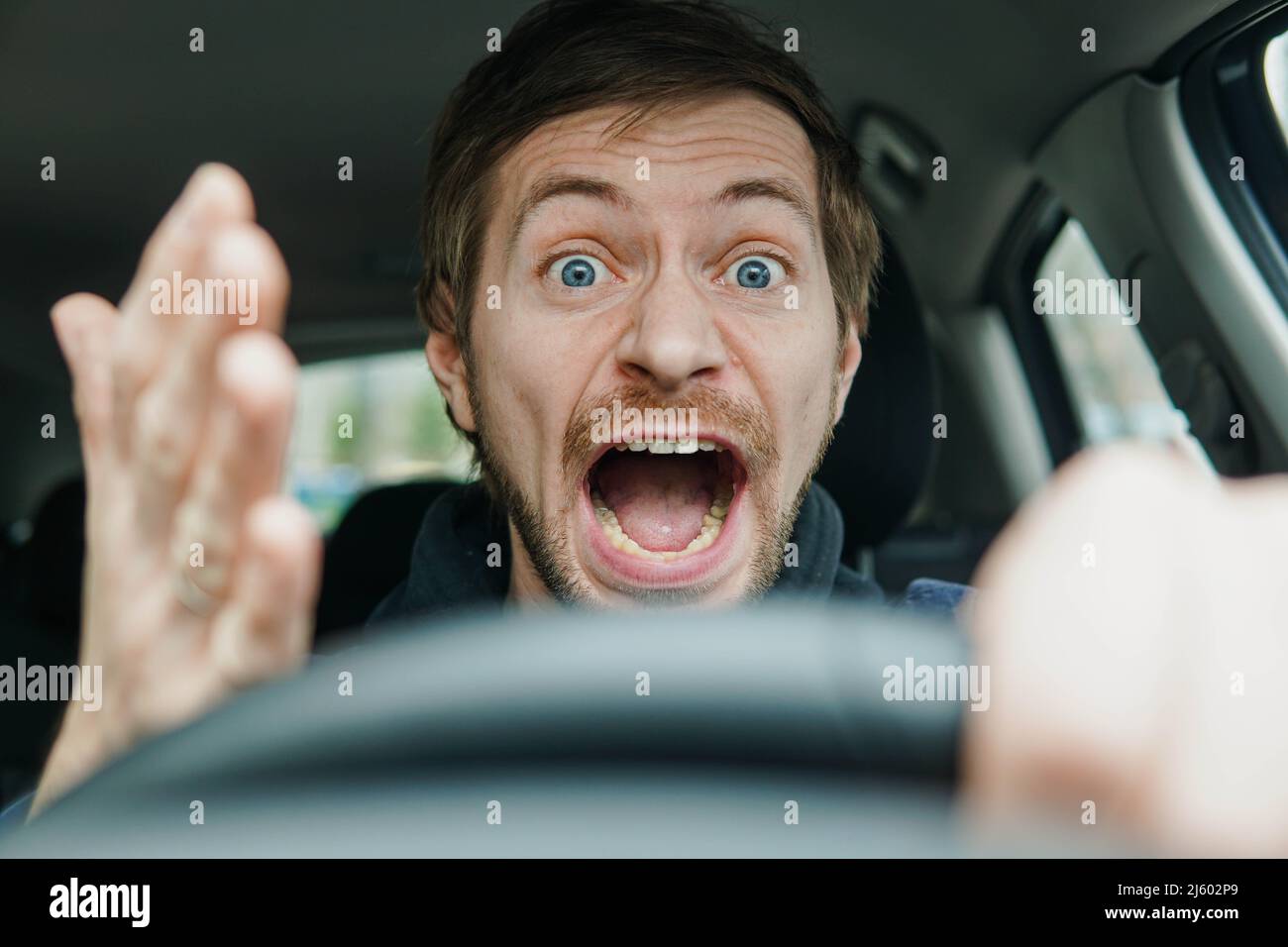 Angry man driving a car. Male driver gesturing and shouting behind the ...