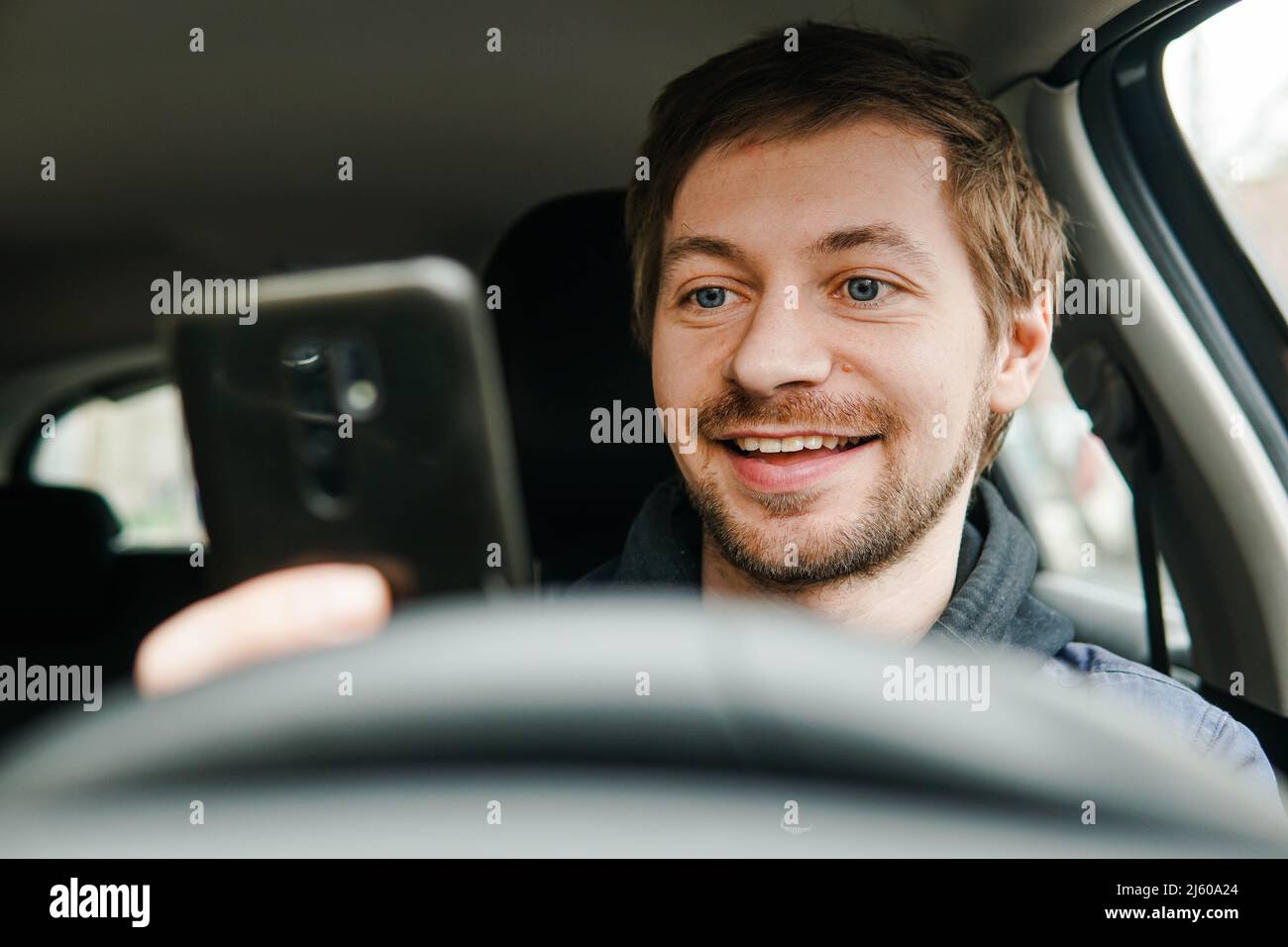 Young smiling male driver using smartphone behind the wheel of the car ...