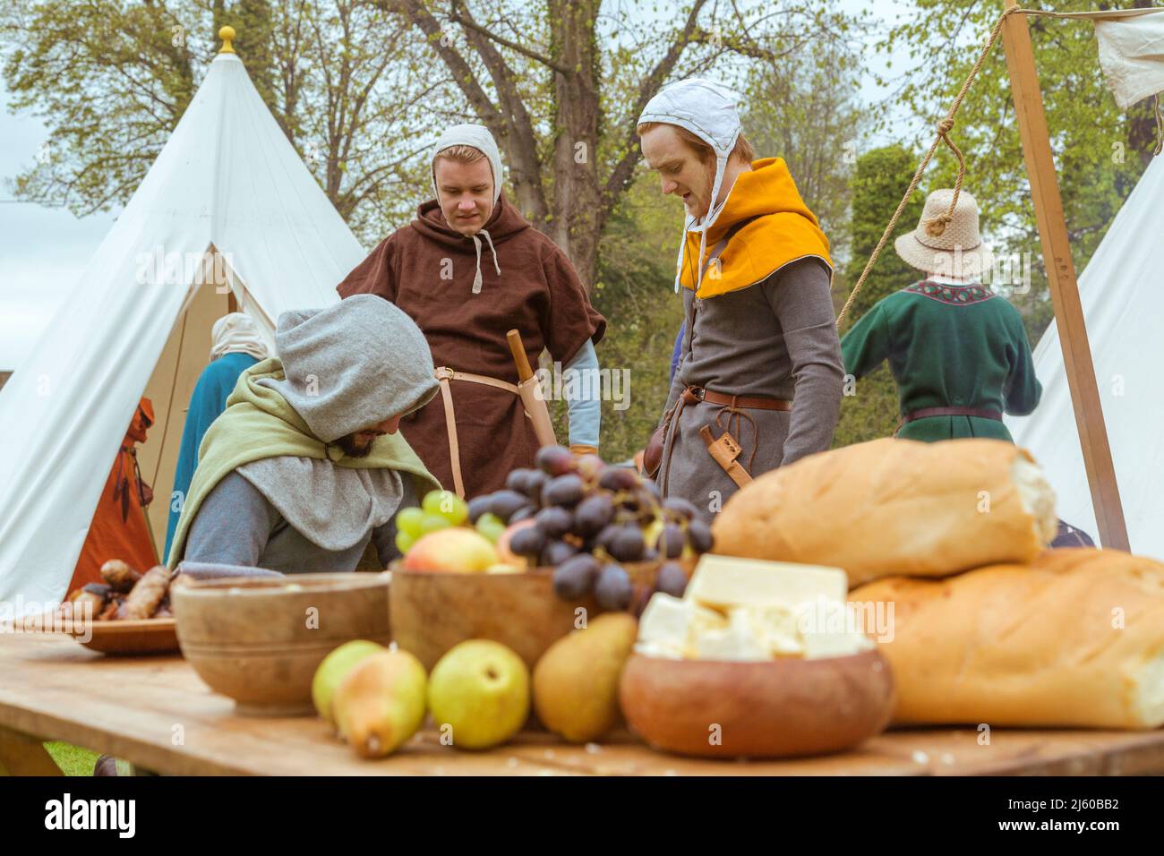 Friends talk by a table of food at a re-enactment of a medieval camp in ...