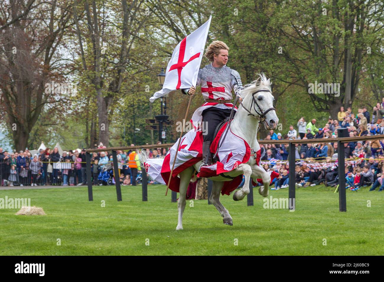 A knight dressed in period costume carries a flag whilst riding a ...
